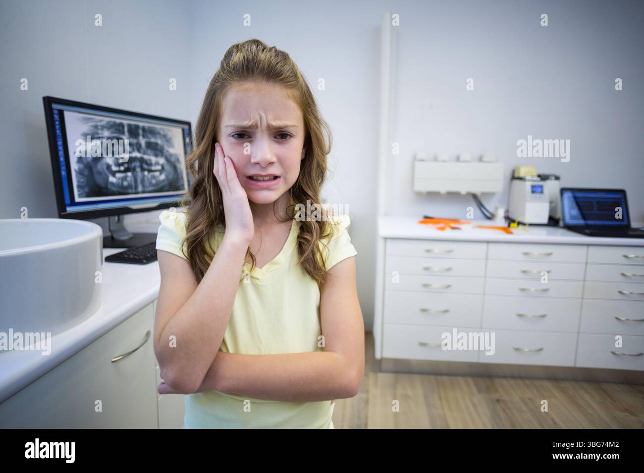 Preteen girl patient pressing hand against cheek in dental exam room ...