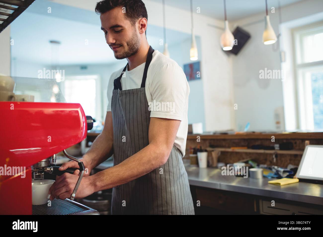 Male barista operating red espresso machine portafilter on counter at ...