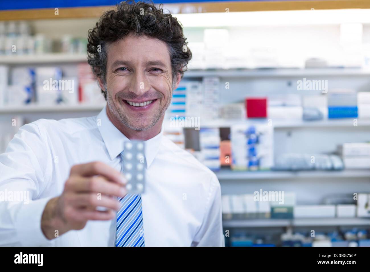 Smiling male pharmacist standing behind counter with medication shelves ...