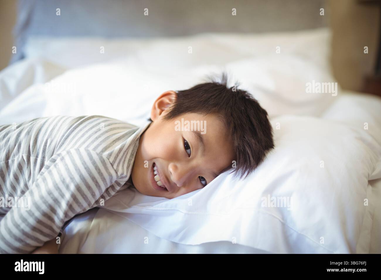 Asian boy lying in bedroom wearing striped pajama top, smiling and ...