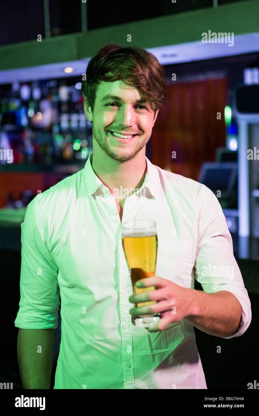 Man holding pint glass at pub counter under green lights, showing ...