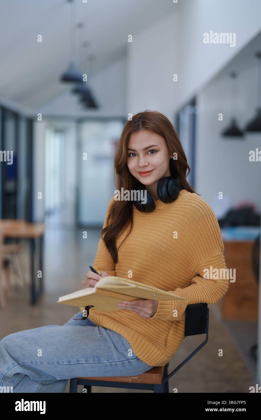 A young woman sits with book and headphones, enjoying study time ...