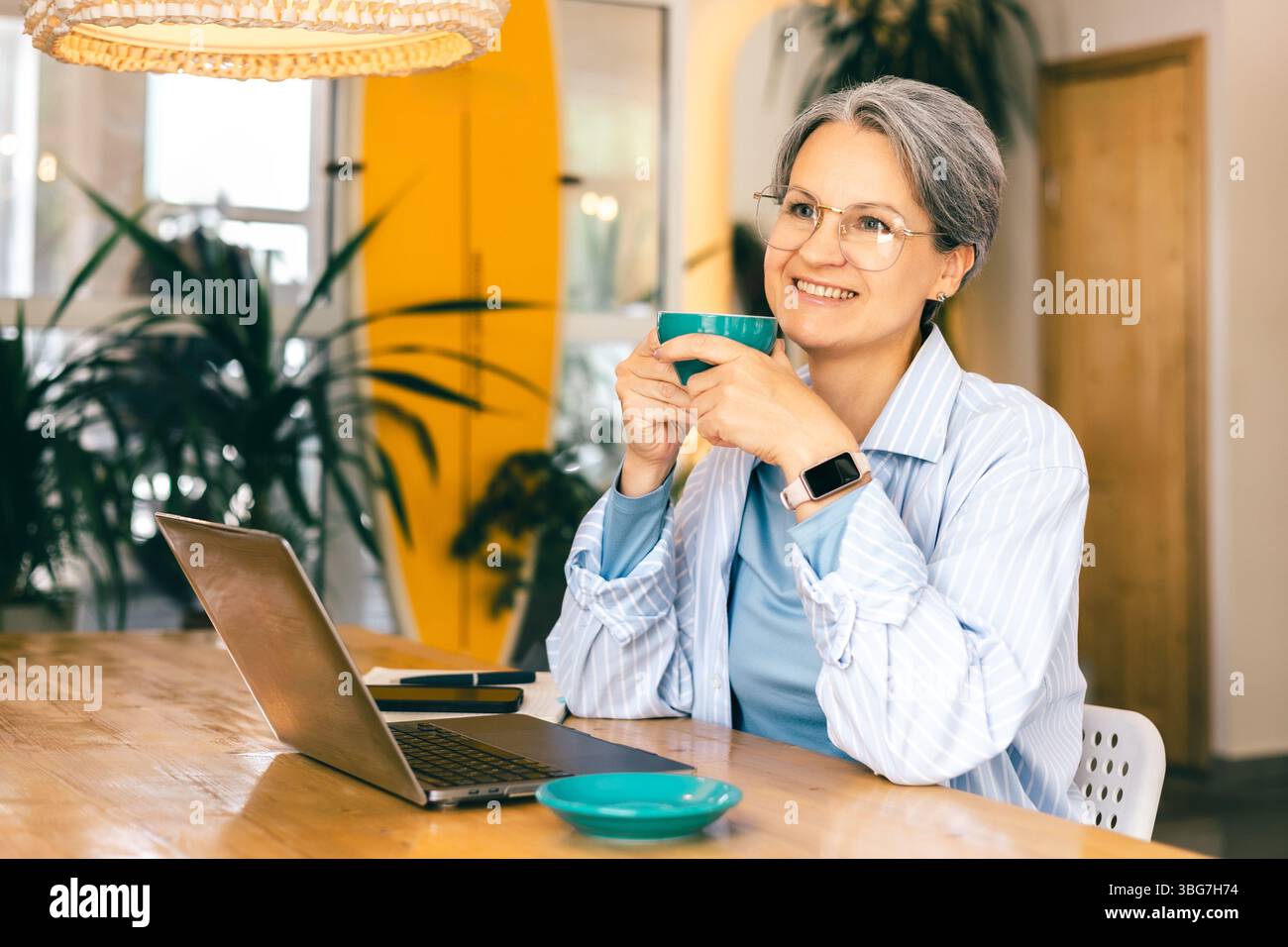 Midlife freelance woman smiling during coffee break while working from ...
