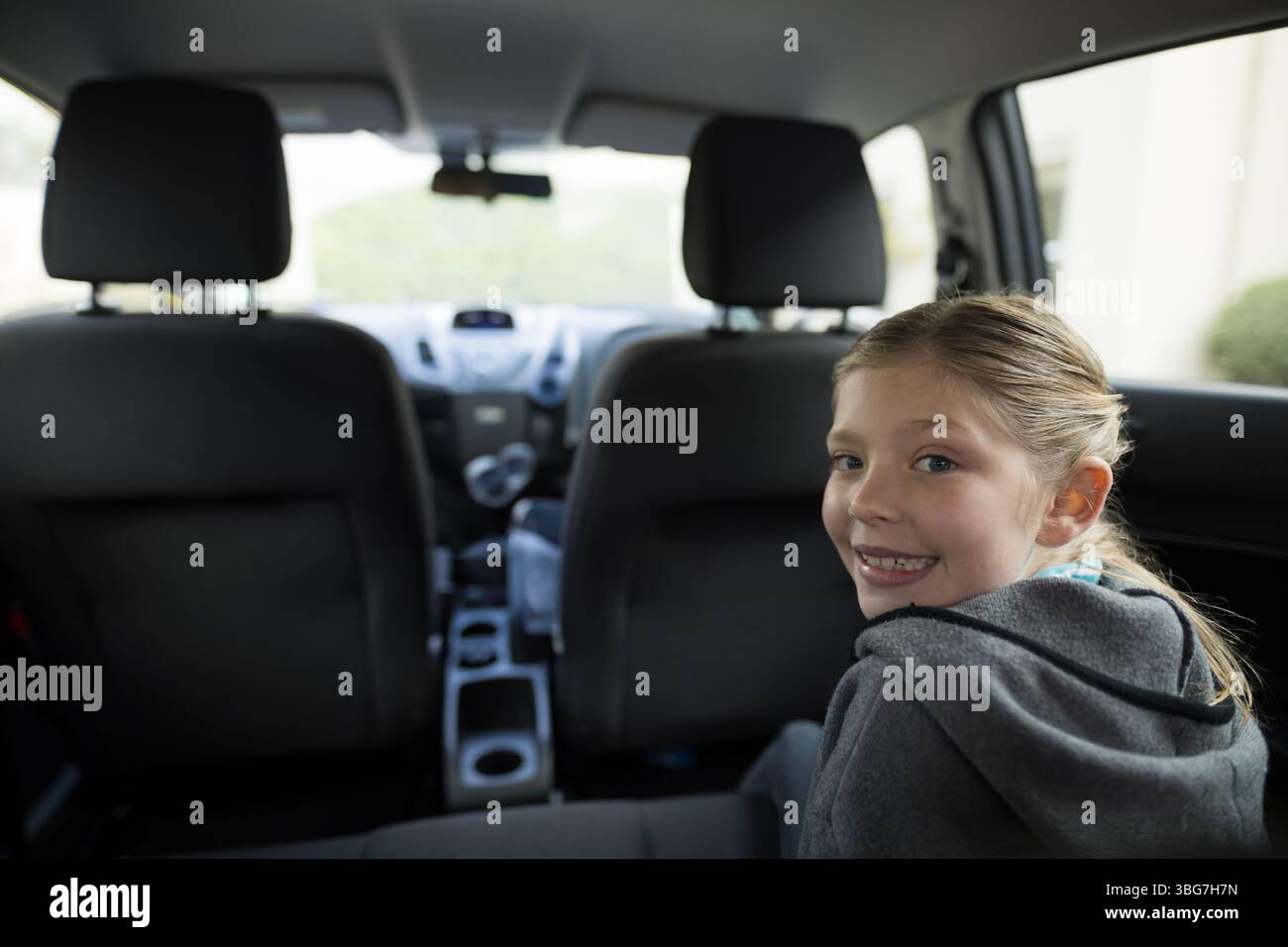 Female child smiling while turning toward camera in car backseat ...