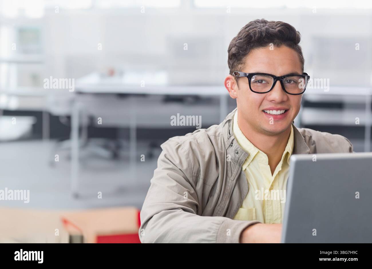 Asian man smiling while typing on laptop at desk in modern office ...