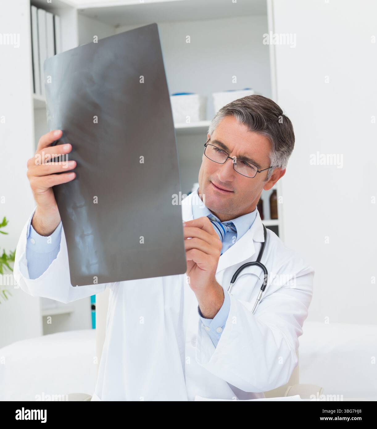 Male doctor holding radiographic film at eye level with stethoscope and ...