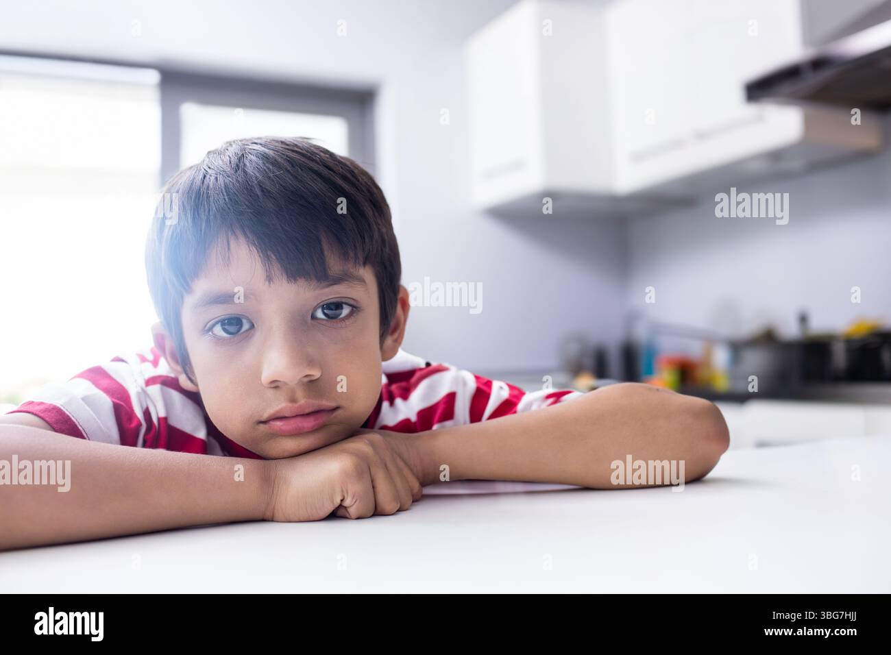 Indian school-age boy wearing striped T-shirt leaning on countertop ...