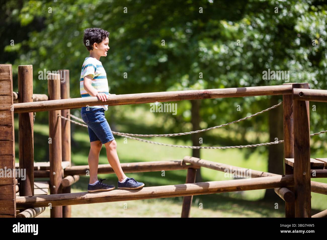 Child balancing on wooden beam while gripping rope handrail in green ...