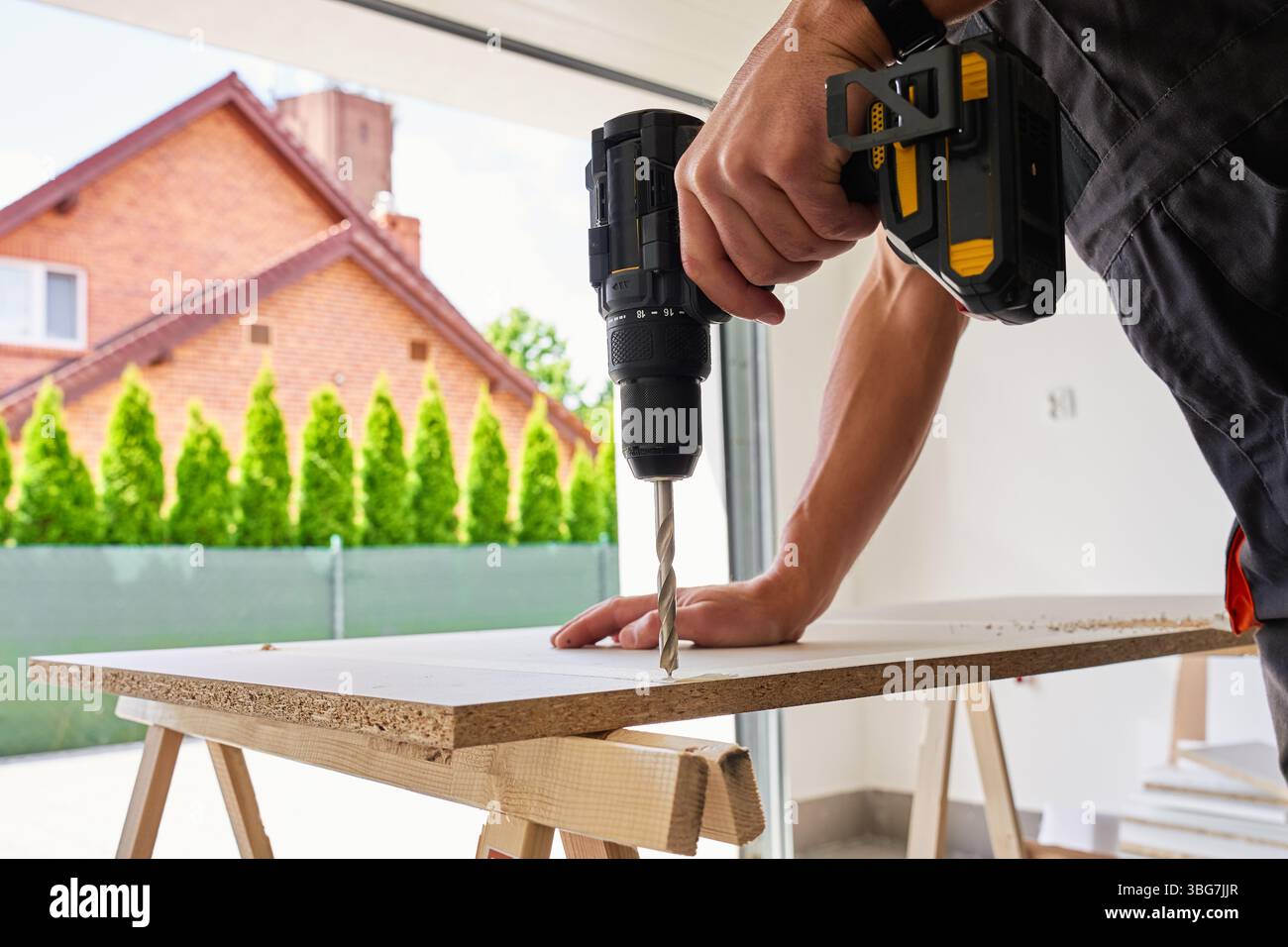Man in work overalls bib using cordless power drill to make hole in ...