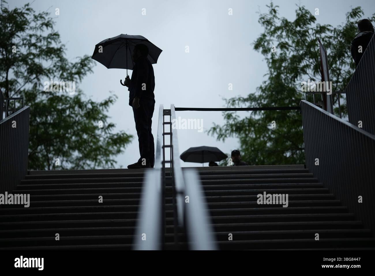 A man stands with an umbrella during a rain at the French Tennis Open ...
