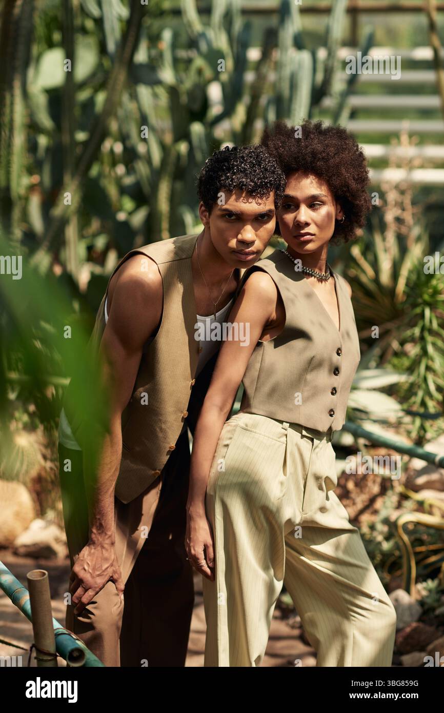 A young couple embraces gently surrounded by lush plants, showcasing ...