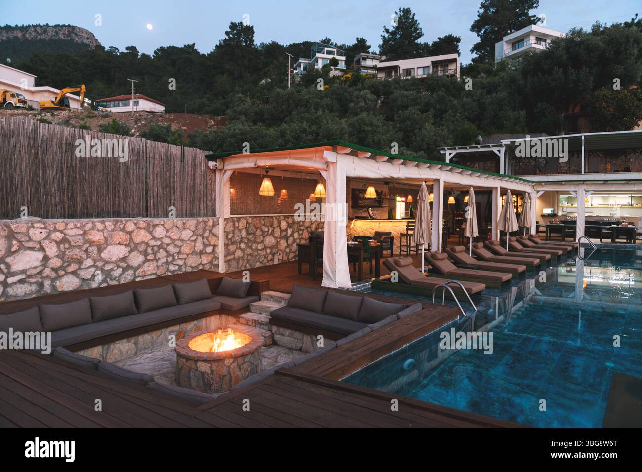A cozy fire pit burns at a luxury hotel with the bar and pool visible ...