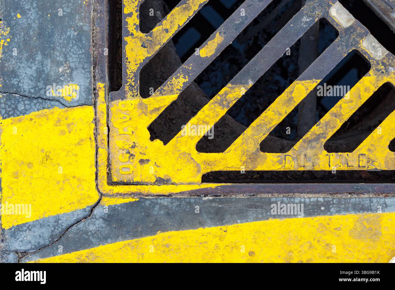 A weathered yellow and gray drainage grate, showcasing the texture and ...
