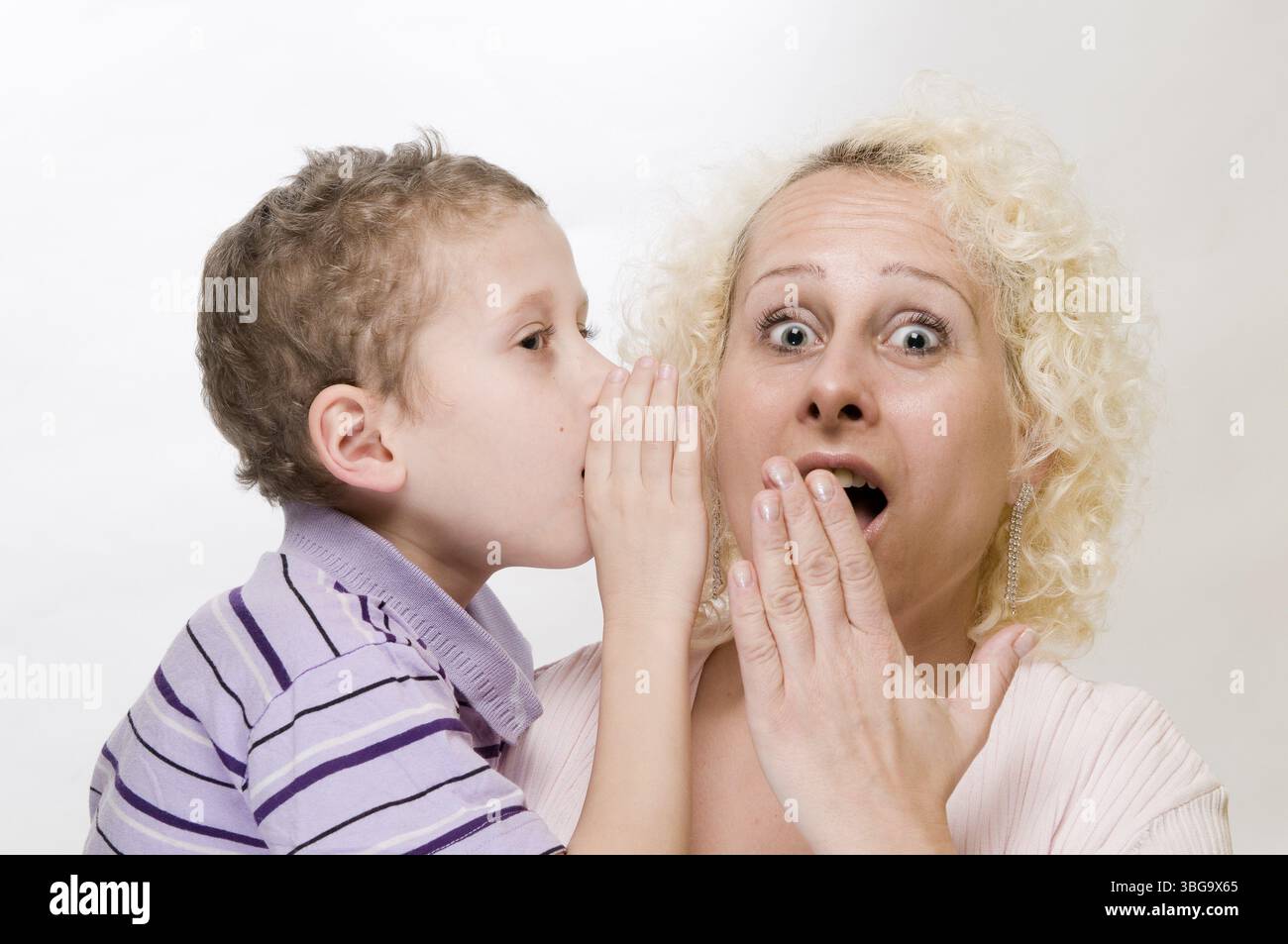 Head-and-shoulders view of a 7-year-old boy whispering into the ear of ...