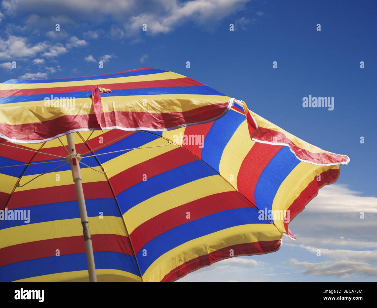Colourful striped parasol from below with blue sky and white clouds ...