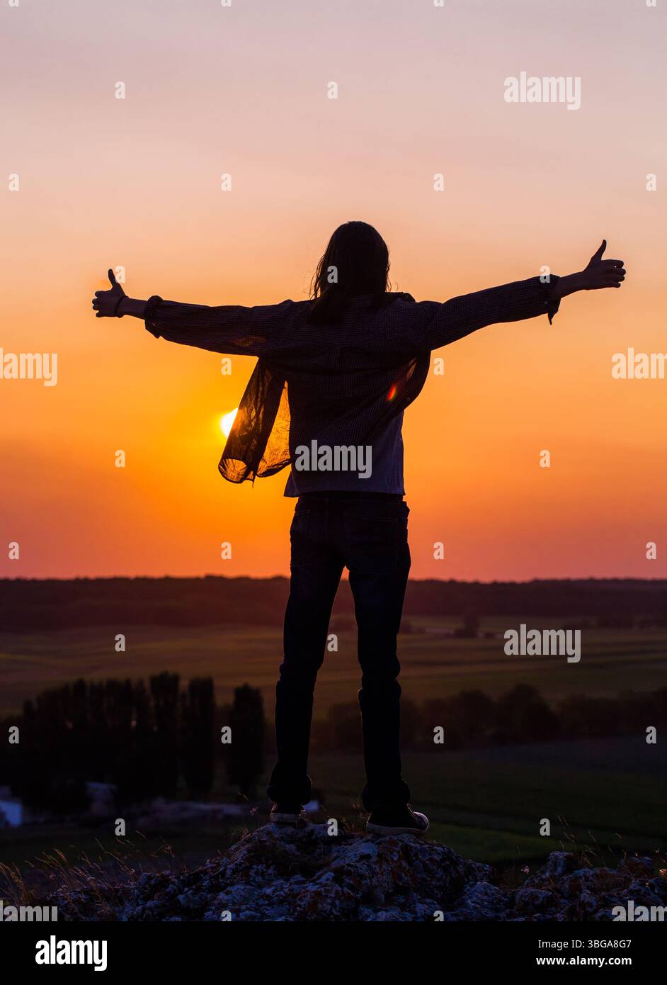 Silhouette of young longhair male model with thumbs-up hands at red and ...