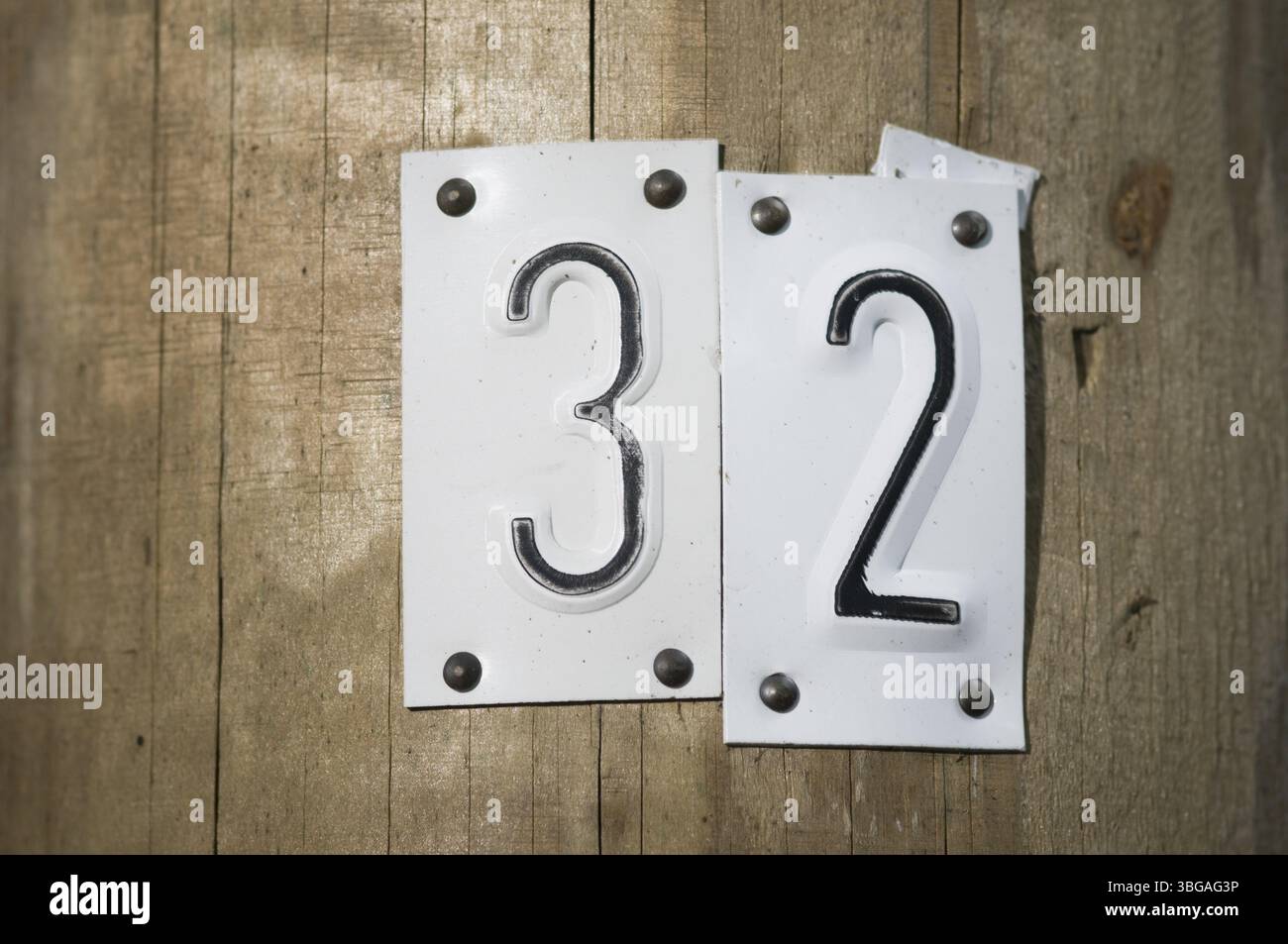 The number 32 embossed in sheet metal (black on white) on a wooden pole ...