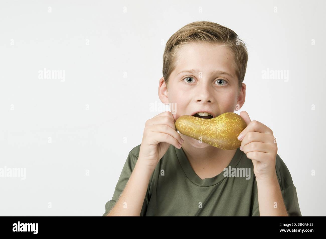 Frontal head and shoulder view of a 13-year-old teenager biting into a ...