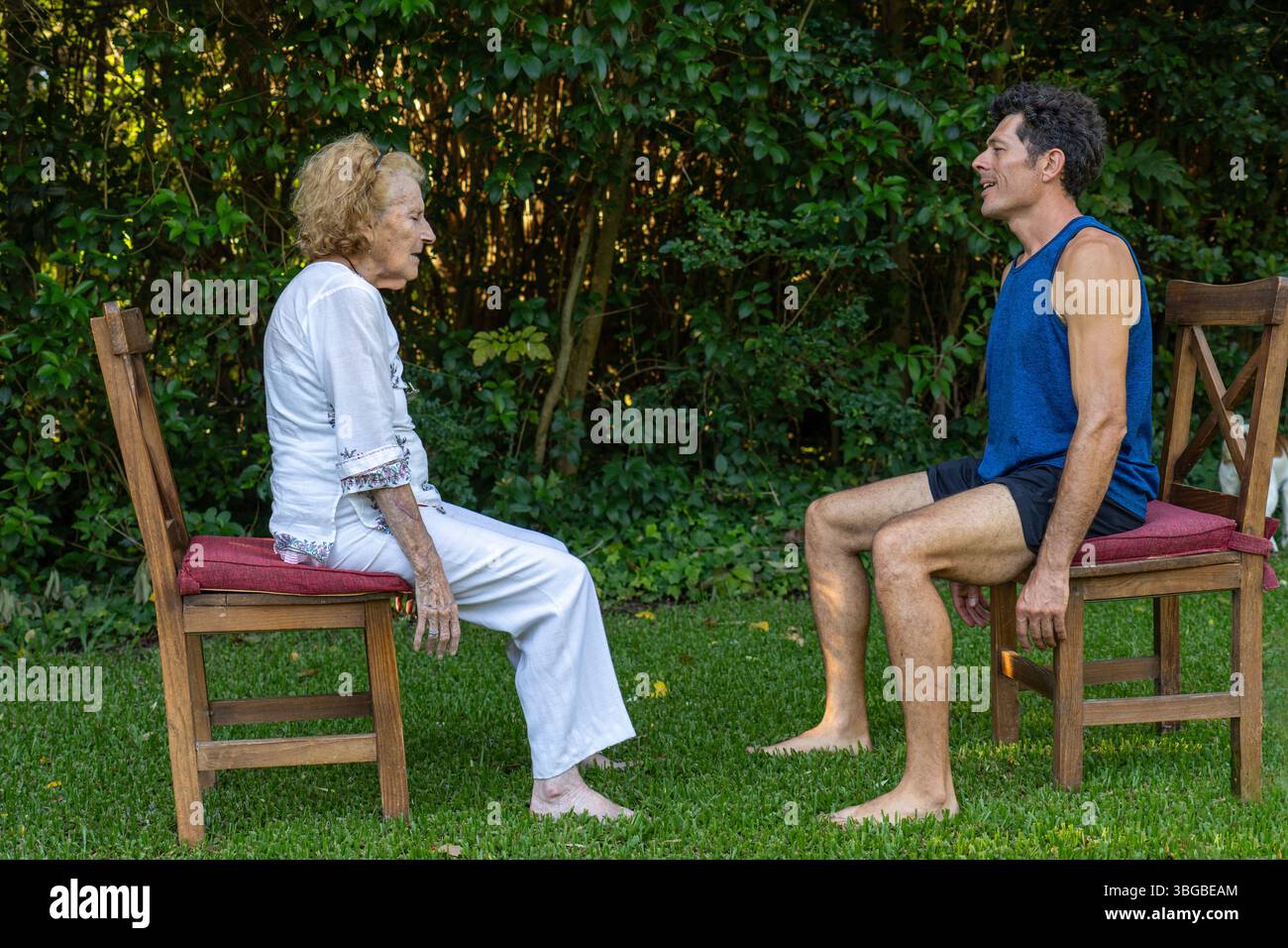Senior woman and her personal trainer practicing rehabilitation exercises sitting on chairs in a ...