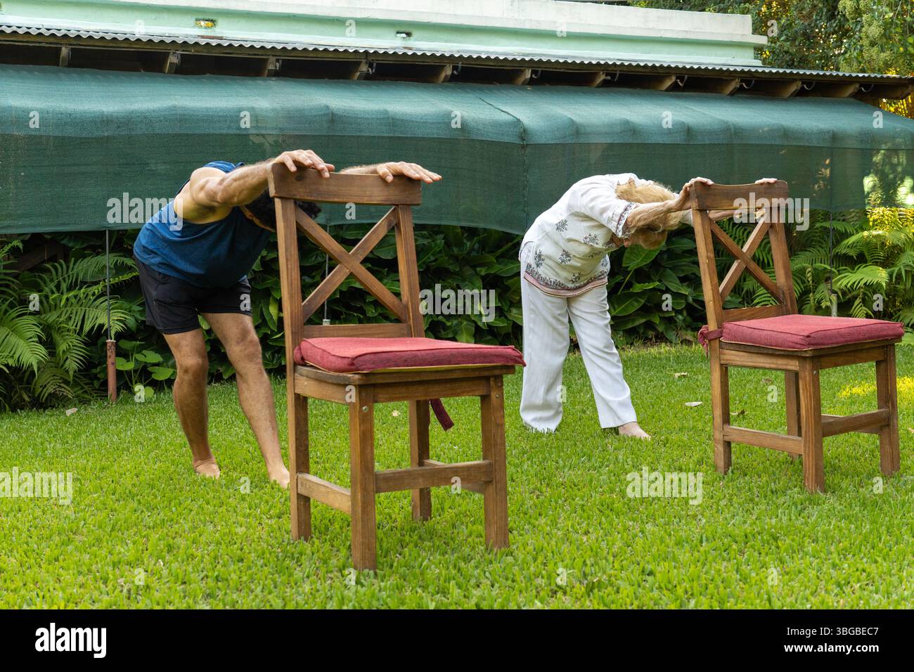 Elderly man and woman practicing stretching exercises with chairs on a ...