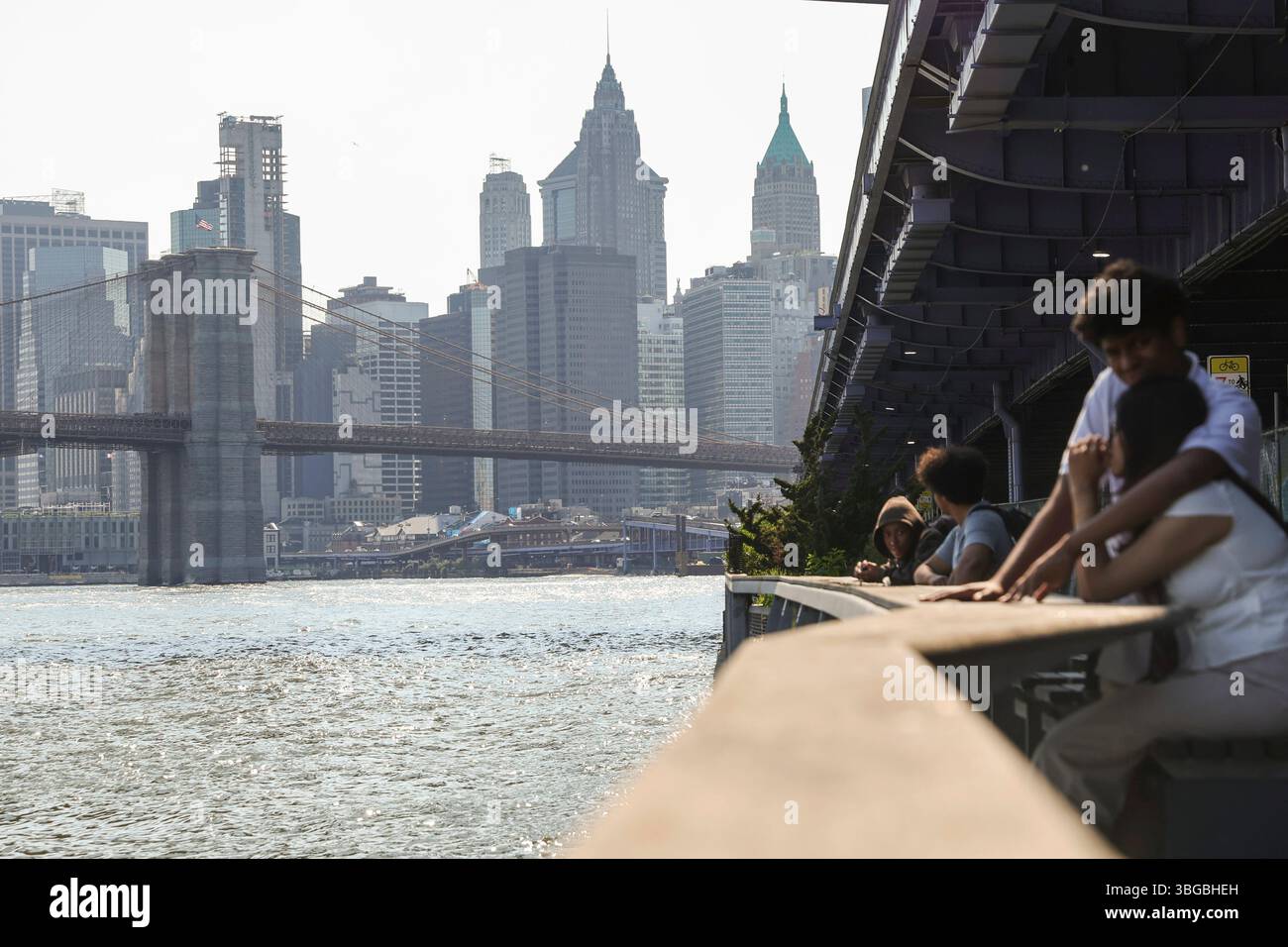 A view of lower Manhattan and the Brooklyn Bridge is seen as people sit ...