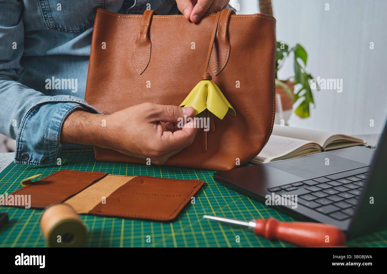 Craftsman adding a yellow leather flower to a brown leather tote bag in ...