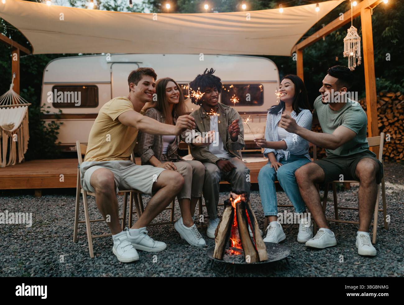 Millennial diverse friends sitting near bonfire with lit sparklers ...
