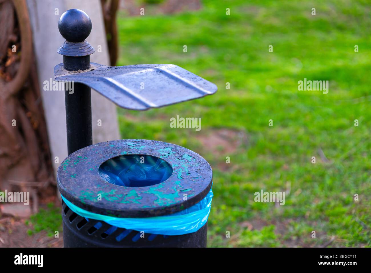 Detailed view of a weathered black metal trash bin with a blue liner ...