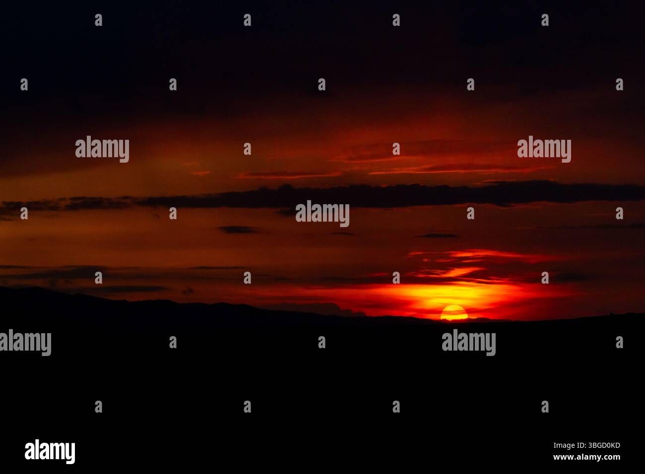 Fiery red sunset over mountains with layered clouds and dark sky ...