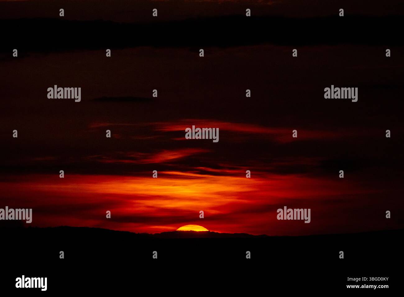 Sun almost fully gone beneath horizon with dark crimson clouds above ...