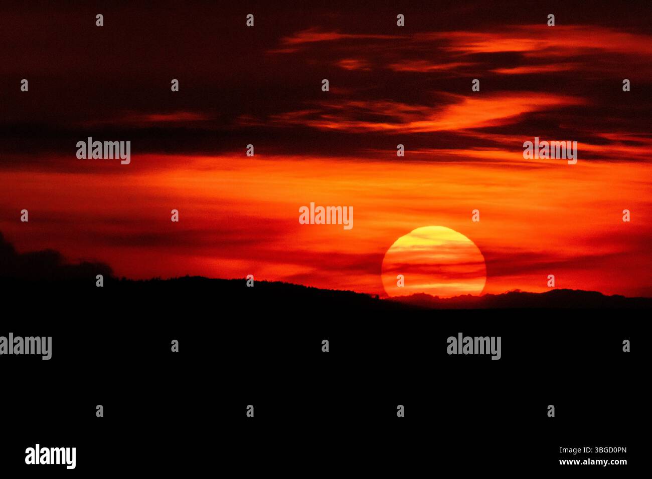A fiery red sunset over a distant mountain ridge, with glowing clouds ...