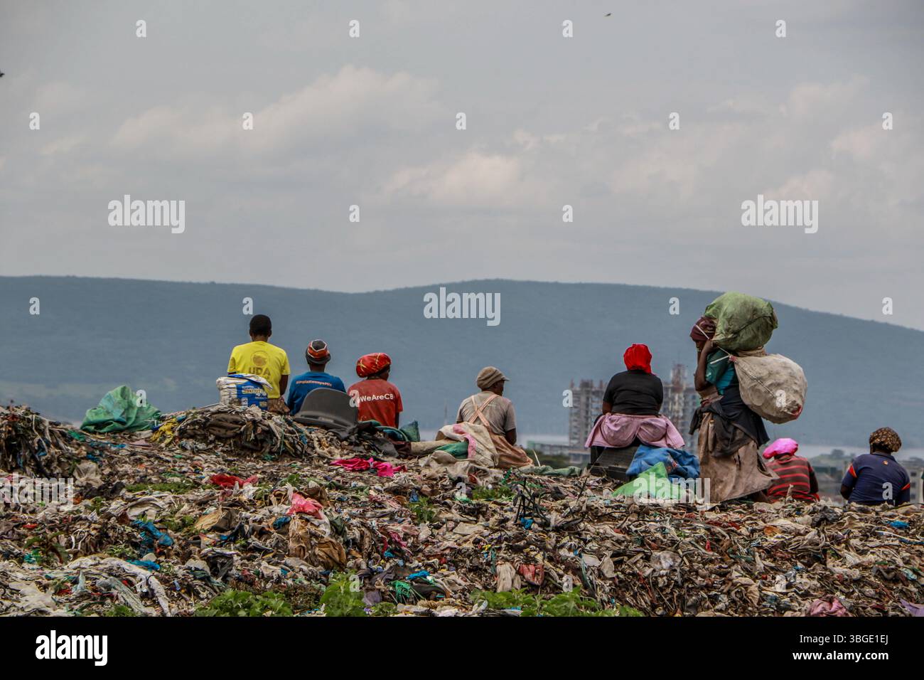 An informal waste worker carries materials to recycle on her back as ...