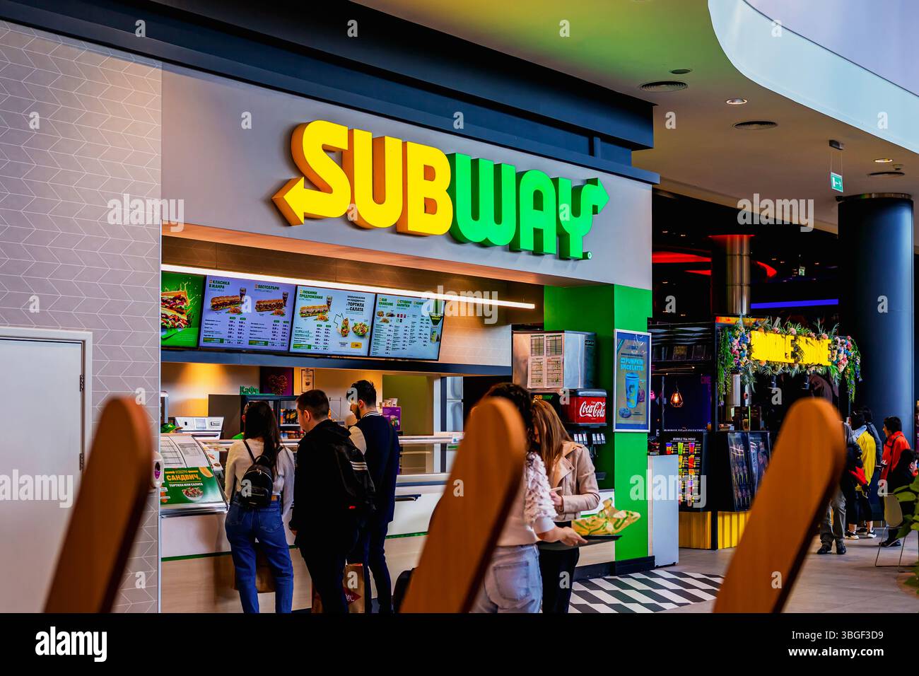 Subway restaurant with bright logo, digital menu boards, and customers ...