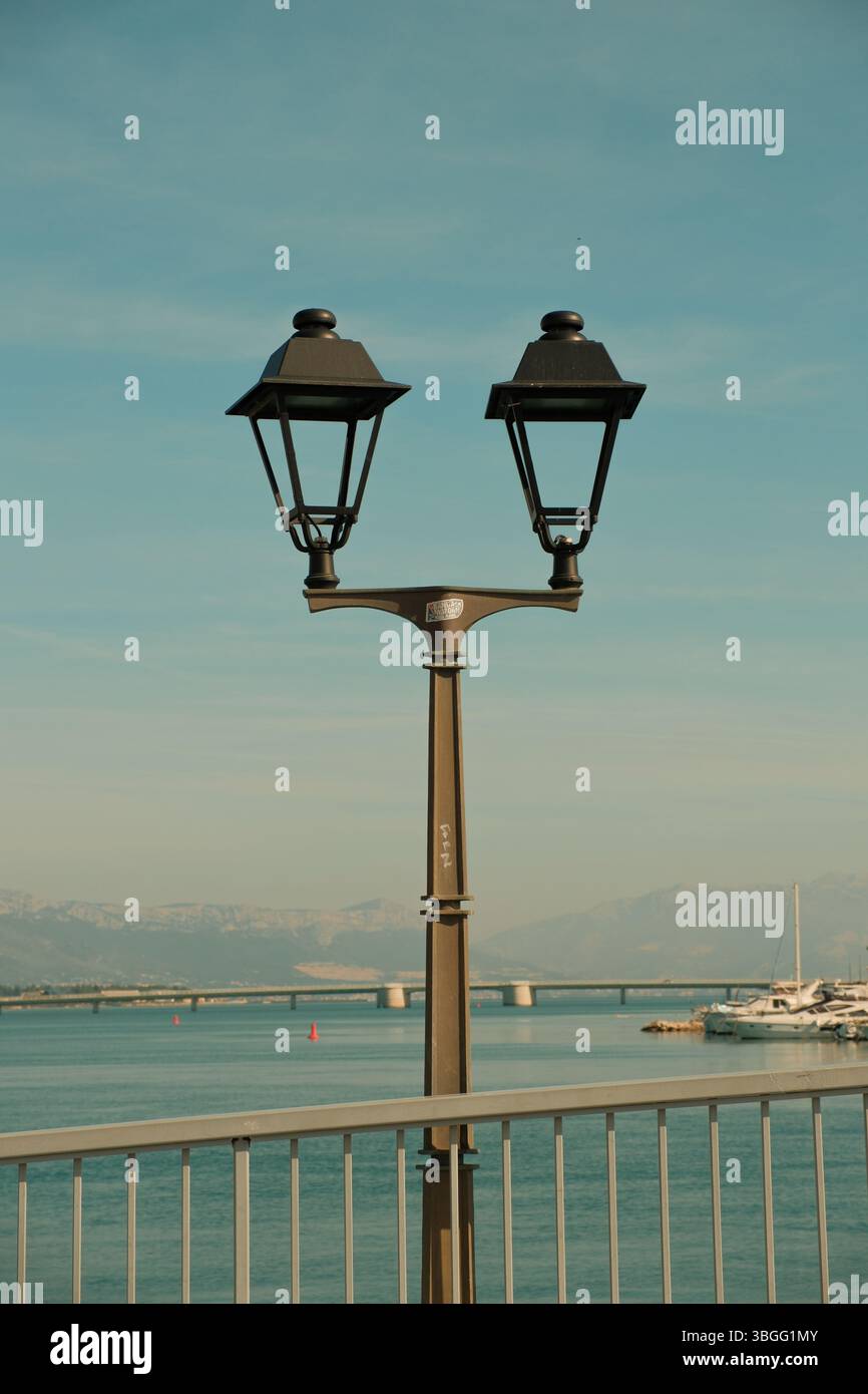 Vintage-style double street lamp by a waterfront railing with mountains ...