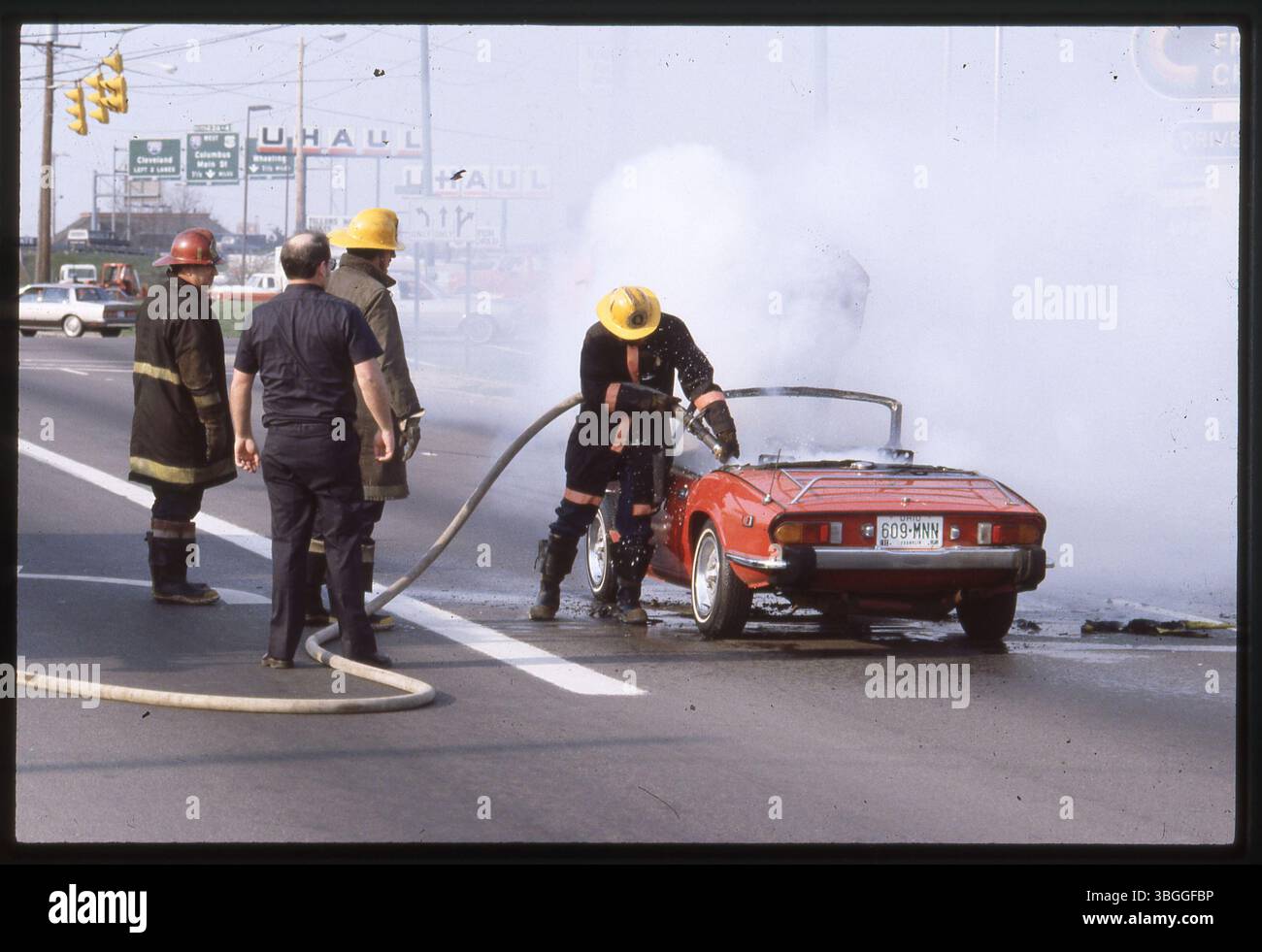 Circa 1982 image showing firefighters extinguishing a car fire. Flames ...