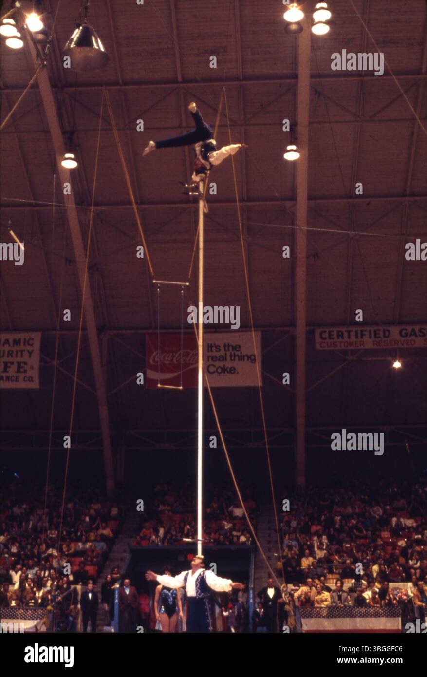 A performer balances a tall pole on his head with another performer ...