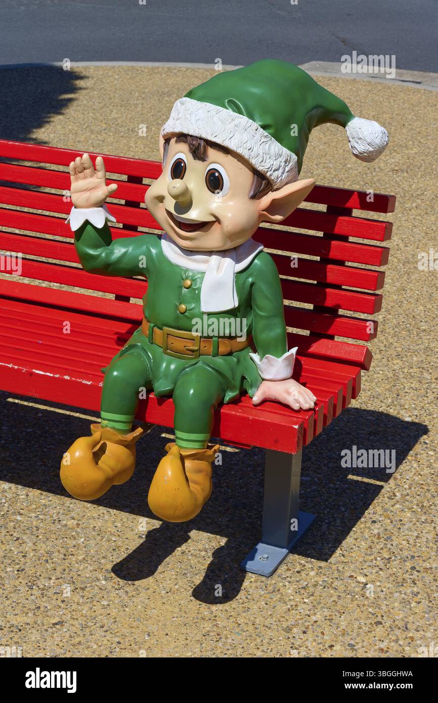 Elf figure in green costume greeting on a red bench in sunny weather ...