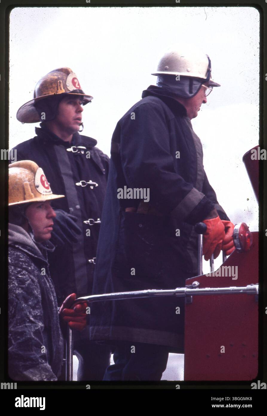 This 1977 photograph features three firefighters standing on a fire ...