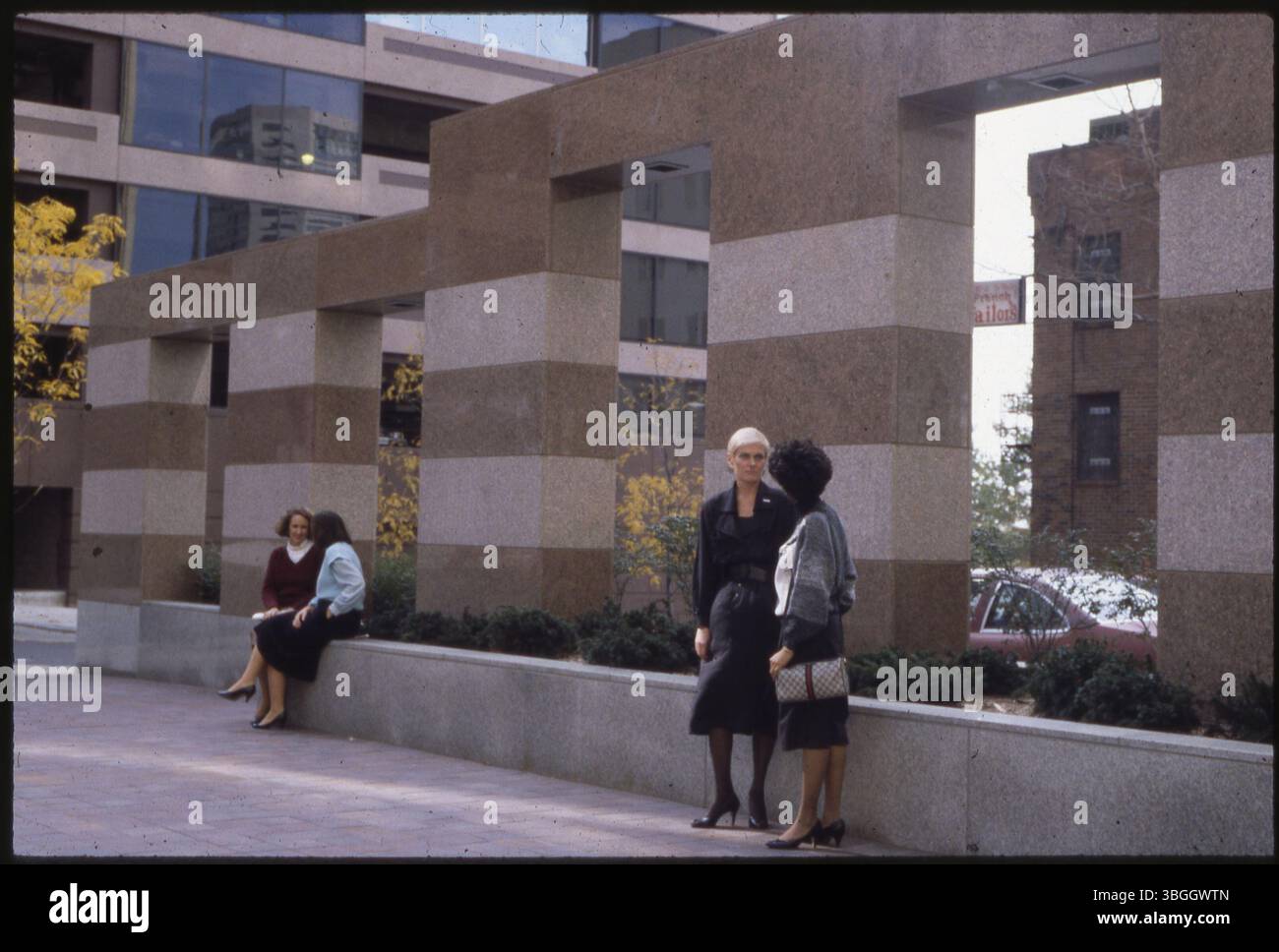 Two women in business attire converse while two others sit on a bench ...