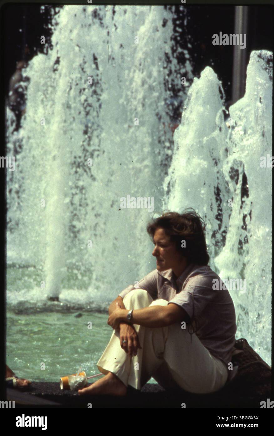 An individual sits near the fountains outside the entrance to the Bank ...