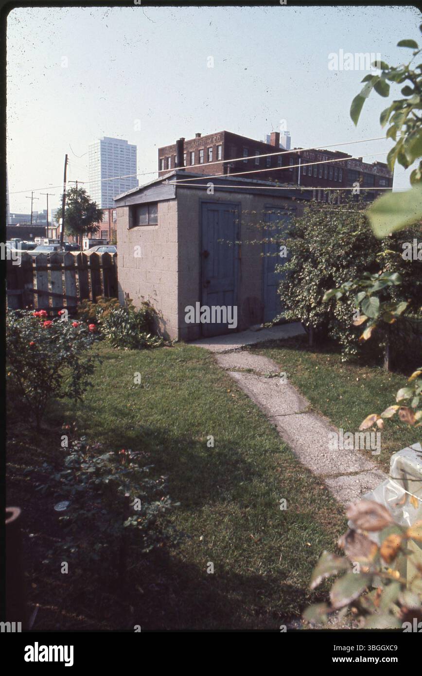 A concrete block shed is located in a fenced yard with an asphalt path ...
