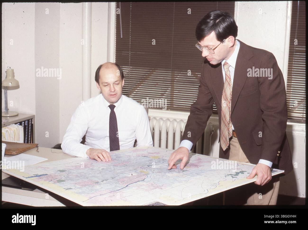 Two men examine a large fold-out map of the Columbus area on an office ...
