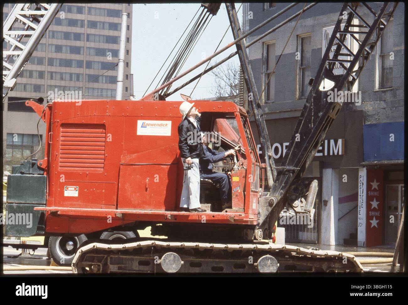 A red Loewendick crane is operated by one man, while a second man ...