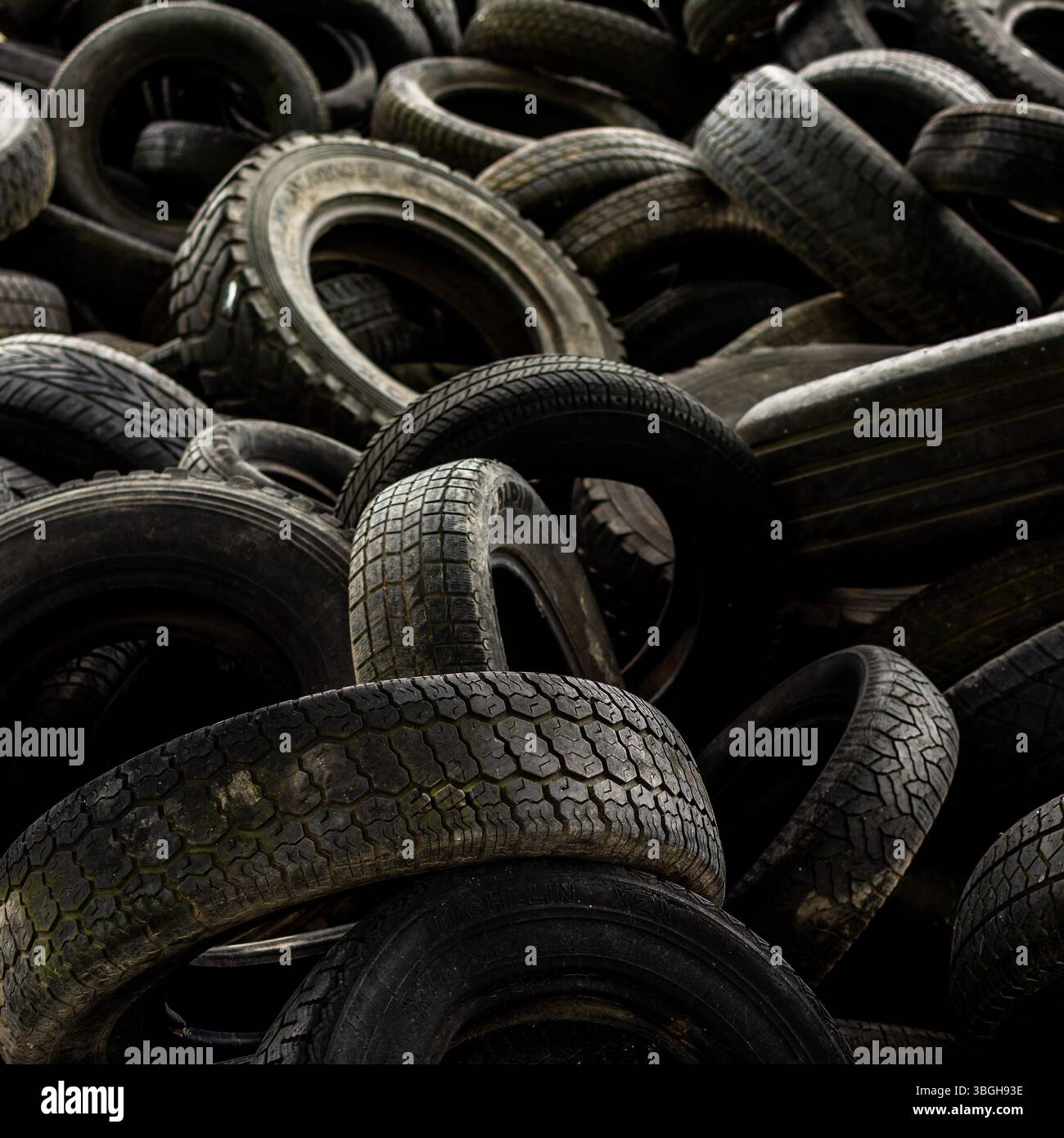 A large collection of worn-out tires is stacked chaotically in a ...