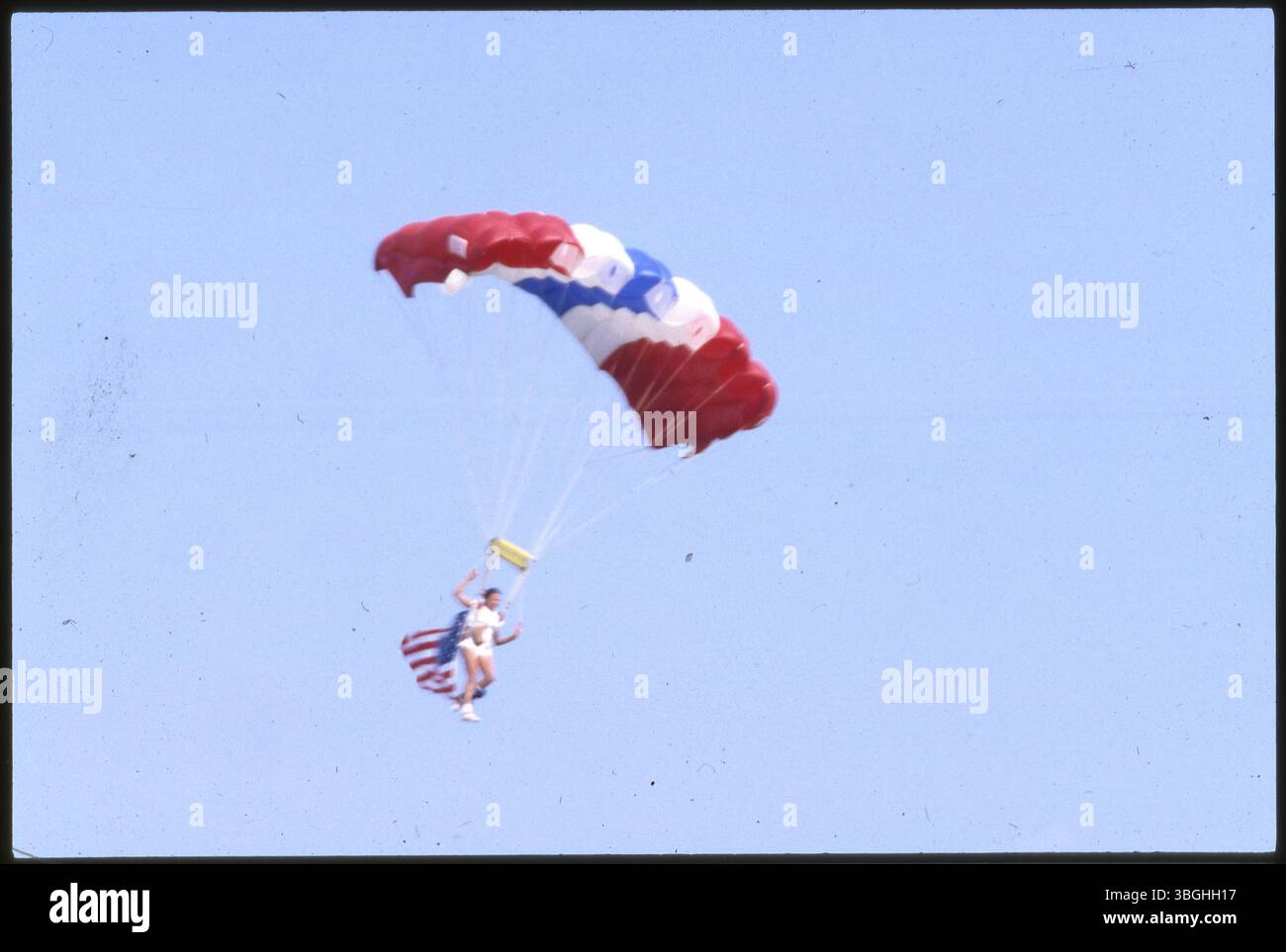 A female parachutist descends with a red, white, and blue parachute ...