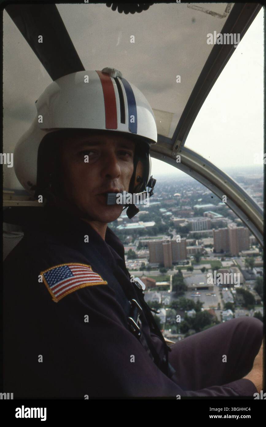 A helicopter pilot is shown in flight with a scenic aerial background ...