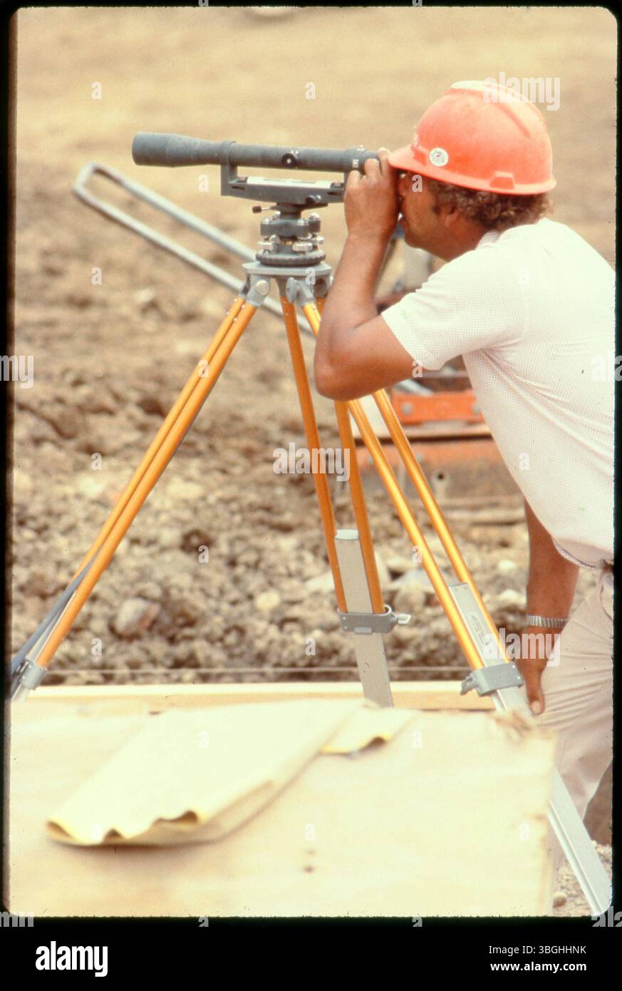 A surveyor in a hard hat uses a theodolite to measure angles on a ...