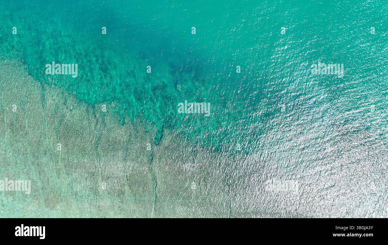 Aerial view reveals the vibrant transition from clear blue sea to sandy ...