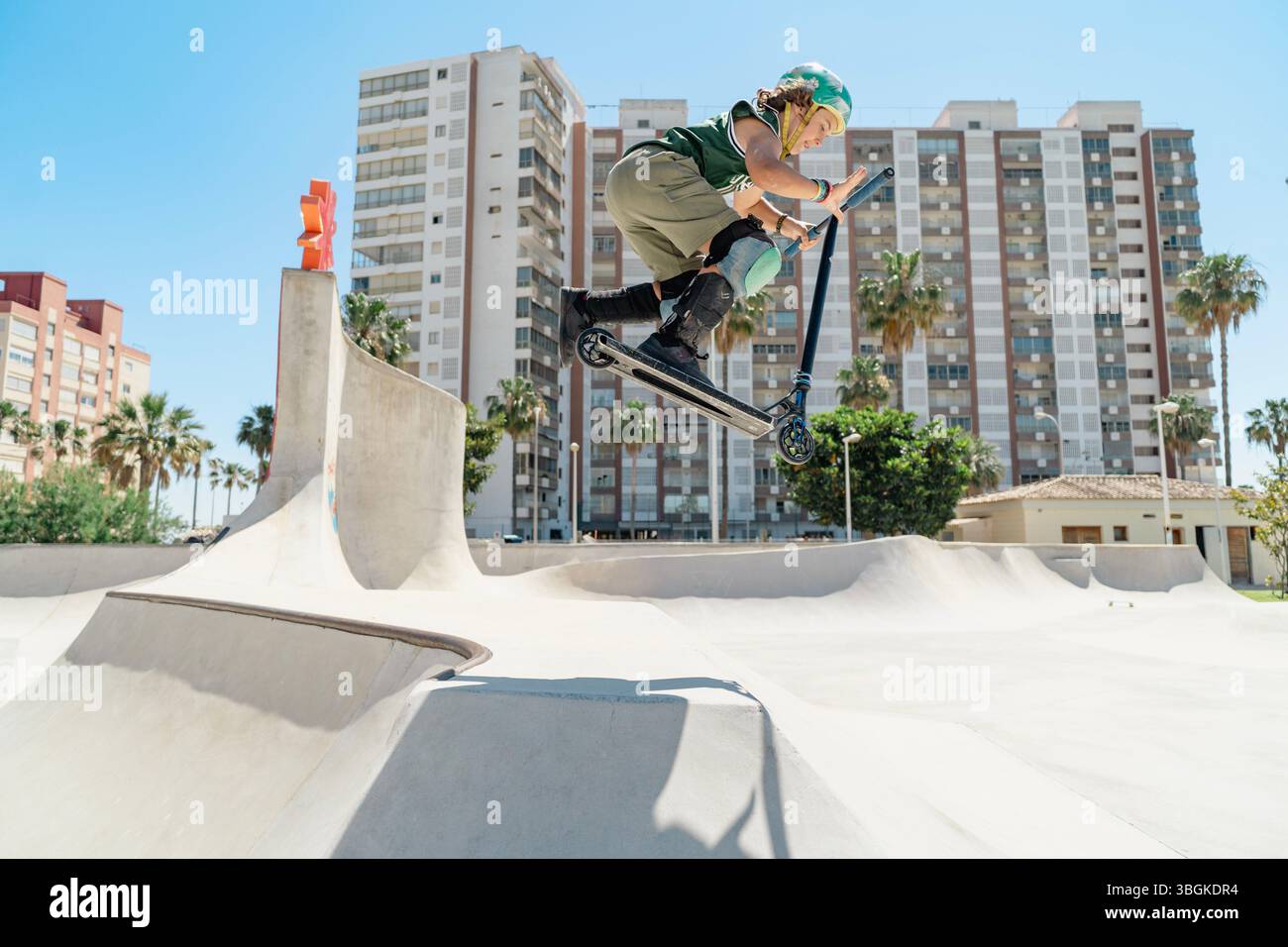 Teenager practicing scooter tricks at a skatepark, jumping high and ...