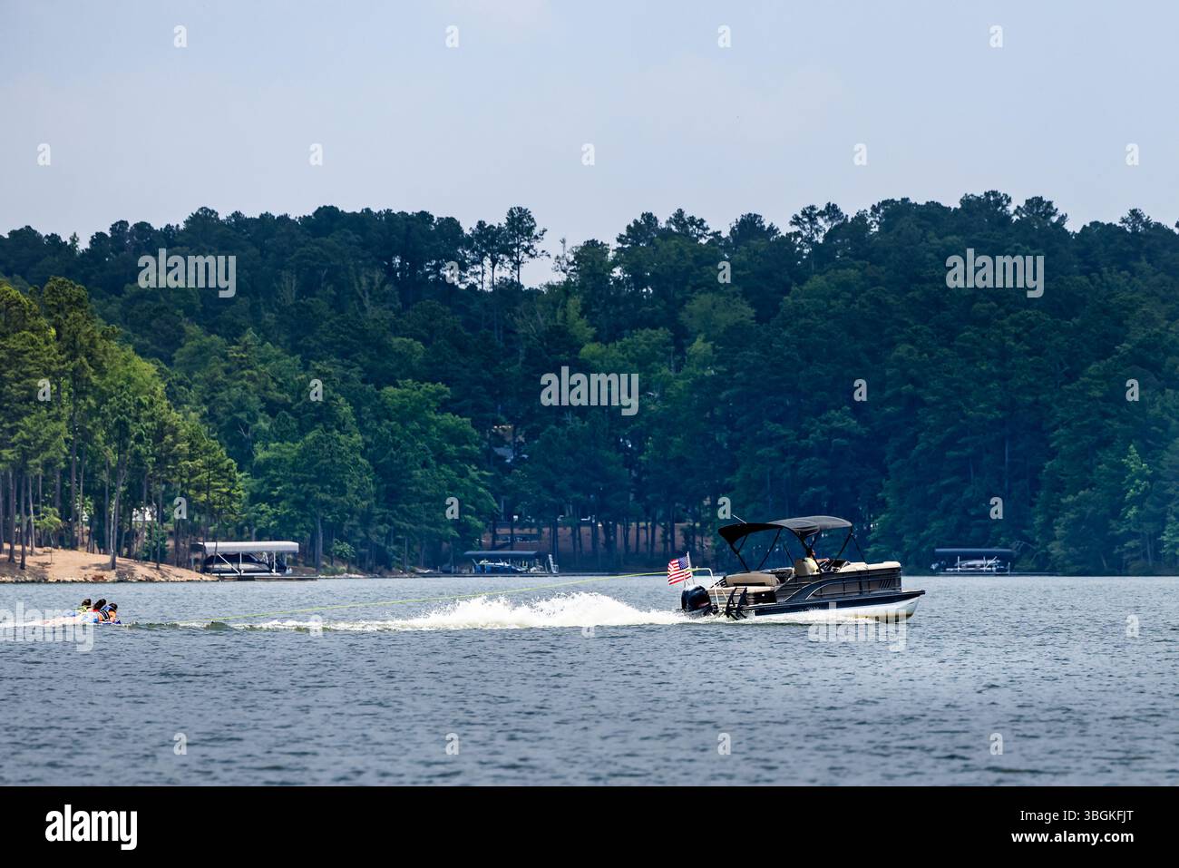 Pontoon boat pulling inflatable tube float raft on lake. Family on a ...